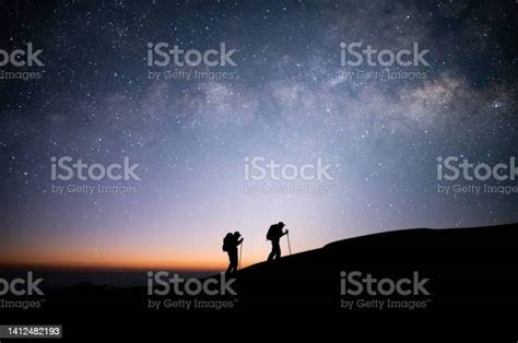 두 명의 젊은 여행자와 배낭 여행자의 실루엣이 아름다운 전망의 별 하늘 위의 은하수로 산 꼭대기로 하이킹을합니다 그는 여행을 즐겼고 정상에 도착했을 때 성공했습니다 2명에