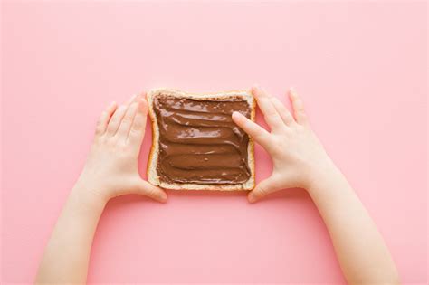 밝은 분홍색 테이블 배경에 갈색 초콜릿 크림과 흰색 빵의 신선한 조각을 만지는 아기 소녀 손 파스텔 색상 근접 촬영 관점 샷 달콤한 간식 하향 보기 초콜릿에 대한 스톡 사진