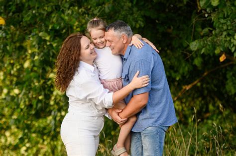 딸을 팔에 안고 함께 시간을 즐기고 웃고 포옹하는 부모는 공원에서 야외 레크리에이션을 즐깁니다 행복한 가족 개념 휴가 가족의