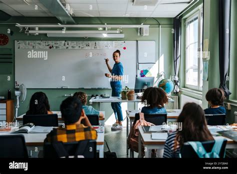 Female Teacher Teaching Mathematics On Whiteboard To Group Of Multiracial Students In Classroom
