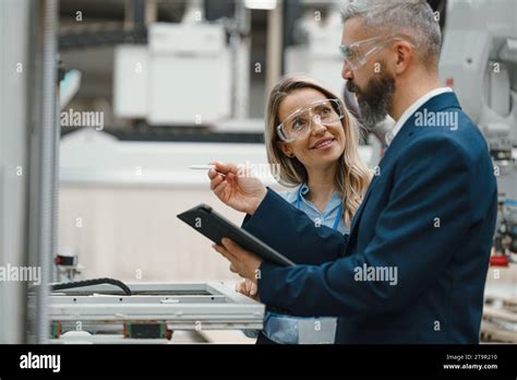 Female Engineer And Male Project Manager Standing In Modern Industrial Factory Talking About