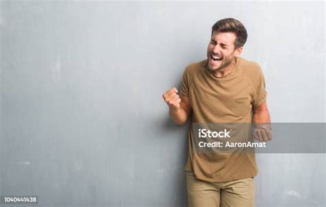 잘생긴 젊은 남자 매우 행복 하 고 흥분 무기와 우승자 제스처를 하 고 회색 그런 지 벽에 웃 고 성공을 위한 비명 축 하 개념입니다 긍정적인 감정 표현에 대한 스톡 사진
