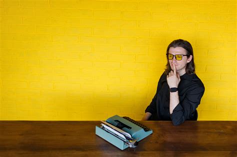 노란 안경을 쓴 한 남자가 타자기 근처의 나무 테이블에 앉아 서서 생각하고 텍스트를 위한 장소를 마련했습니다 기계류에 대한 스톡 사진 및 기타 이미지 Istock