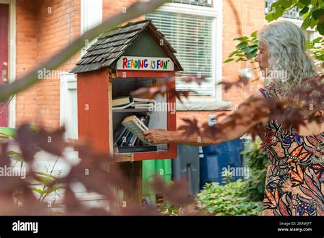 A Woman Checks Out Free Books At A Front Yard Little Library Which