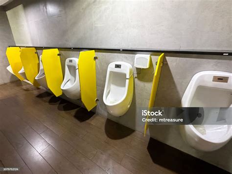 공중 화장실 화장실에 줄지어 있는 흰색 세라믹 소변기 그릇에 담긴 향기로운 소변기 노란색 플라스틱 프라이버시 스크린 파티션 배경 스플래시 백 벽 내부에 배수구와 배수구가