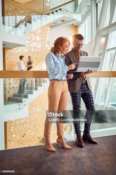 한 사업가가 회사 건물 복도에 서있는 동안 젊은 남성 동료가 그녀에게 보여준 노트북 콘텐츠를보고 있습니다 비즈니스 사람 회사 사무실에 대한 스톡 사진 및 기타 이미지