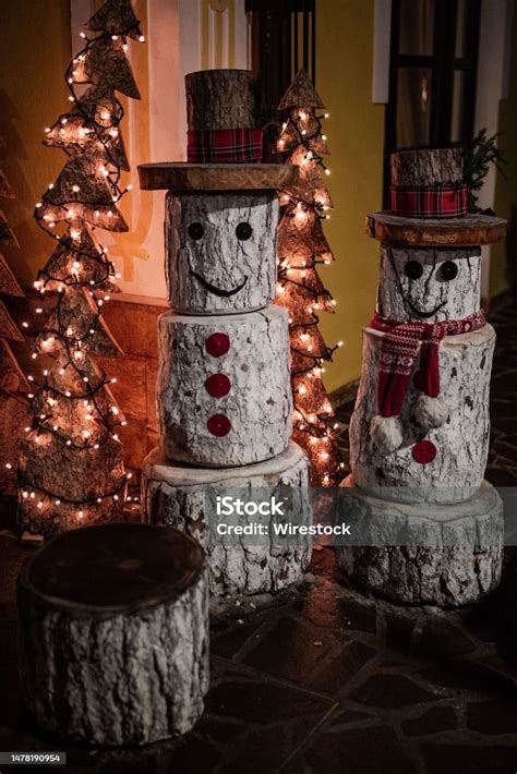 나무 통나무로 만든 눈사람 모자를 쓰고 조명이 켜진 크리스마스 트리 옆에 서 있는 사람 겨울에 대한 스톡 사진 및 기타 이미지 겨울 계절 고드름 Istock