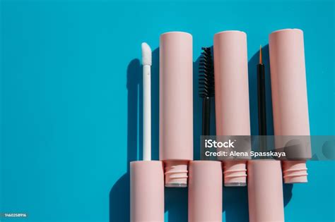 화장품과 브러쉬의 분홍색 튜브가 파란색 배경에 놓여 있습니다 공간을 복사합니다 립스틱의 닫힌 튜브 액체 립글로스 마스카라 아이