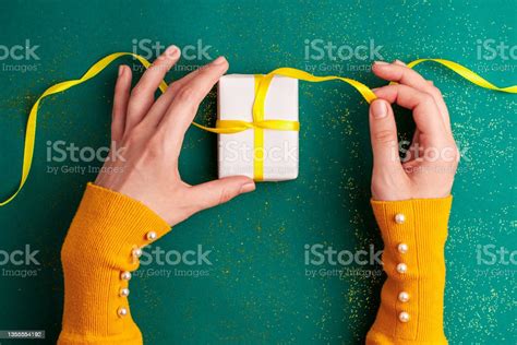 인간의 손은 금색 반짝이가 있는 에메랄드 그린 배경에 노란색 새틴 리본 리본리본이 달린 흰색 선물 상자를 풀었다 크리스마스 휴일 과 현재 개념 플랫 평지 0명에 대한 스톡