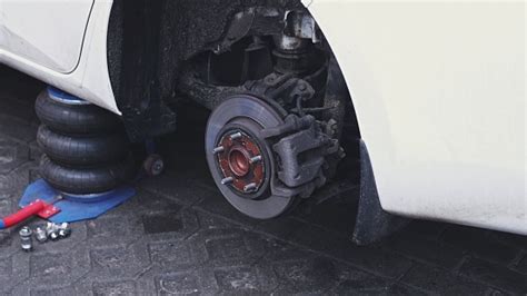 러그 너트와 렌치가 땅에 누워 있는 차고 작업장에서 타이어 교체 중에 브레이크 디스크와 브레이크 패드가 노출된 자동차 휠 허브