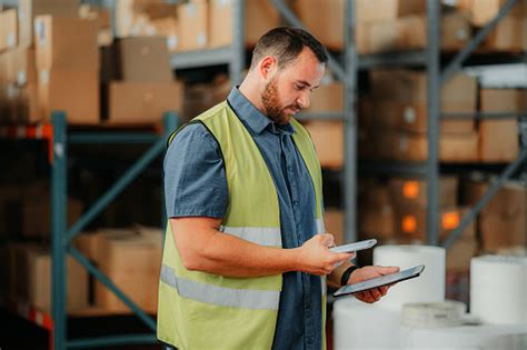 창고 재고 및 휴대 전화 및 태블릿을 가진 남자가 배달을 위해 온라인으로 재고를 확인합니다 기술 화물 및 소매 글로벌 운송 서비스를위한 포장 및 상자에 제품 목록을 가진