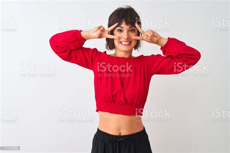 고립 된 흰색 배경 위에 서있는 빨간 여름 티셔츠를 입은 젊은 아름다운 여성은 얼굴에 손가락으로 평화 의 상징을하고 승리를 보여주는 쾌활한 미소 T 셔츠에 대한 스톡 사진