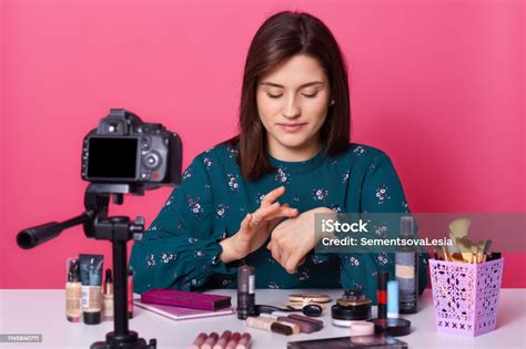 세심 한 검은 머리 블로거는 그녀의 손을 바라보 고 피부를 만지고 피부에 기초를 두고 시청자와 가입자를 테스트 합니다 슬림 귀여운 여자 스튜디오에서 분홍색 배경 위에 고립