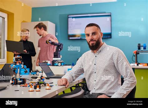 A Man Sitting In A Robotics Laboratory While His Colleagues In The