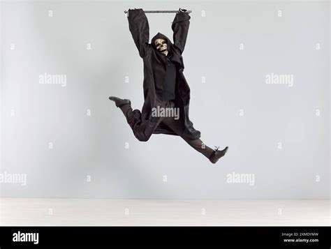 Man In Grim Reaper Death Costume Jumping With Scythe In His Hands And