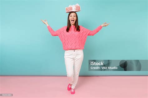 전체 길이 장미 니트 스웨터에 여자의 초상화 흰색 바지 들고 포즈 선물 상자 스튜디오에서 밝은 핑크 블루 파스텔 벽 배경에 고립 패션 라이프 스타일 개념입니다 복사 공간을