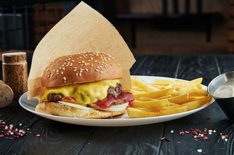 쇠고기 패티 녹은 체다 치즈 베이컨 버섯 토마토 절인 오이 및 감자 튀김과 하얀 접시에 양파와 식욕을 돋 우는 육즙이