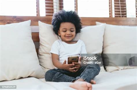 집에서 거실에서 아이들을위한 온라인 응용 프로그램을 즐길 재미를 가지고 만화를보고 스마트 폰을 사용하여 소파에 앉아 아프리카 작은 귀여운 소년 가젯 개념에 중독 된 기술