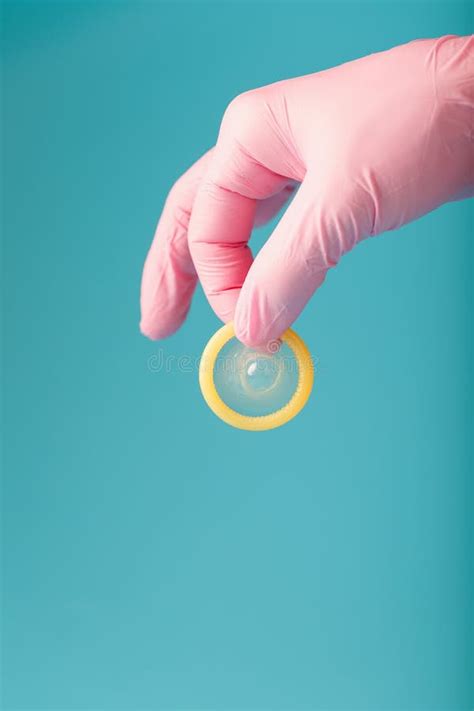 An Opened Condom In A Hand In A Pink Glove Holds On A Blue Background