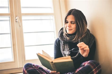 추운 겨울에는 울 모자와 스카프를 들고 책을 읽는 어린 아름다운 소녀 여자는 창 근처에 앉아 있다 집에서 휴식을 취하는 여성 라이프 스타일 잠금 평온과 교육 개념 거실에