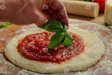 Hand Placing Basil Leaf On Fresh Tomato Sauce Spread On Pizza Dough