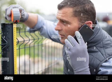 worker installing welded metal mesh fence measuring and calling stock