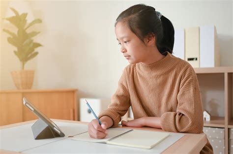 혼자 거실에서 태블릿을 사용하여 온라인으로 공부하는 아시아 어린이 Brand Name Online Messaging