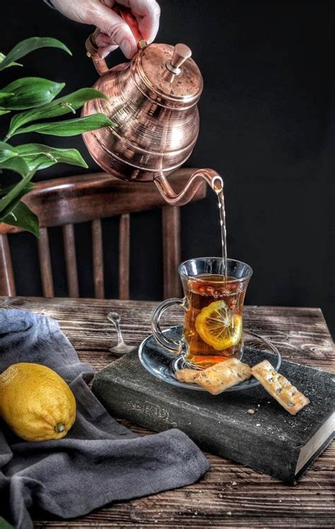a person pouring tea into a glass cup with lemons and crackers on the side