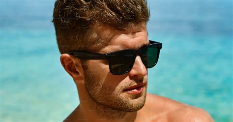 여름에 남자 스킨 케어 선글라스를 끼고 섹시한 몸매를 가진 잘생긴 남성이 일광욕을 하기 전에 자외선 차단 자외선 차단제 로션을 바르고 건강한 황갈색을 위해 태양 자외선