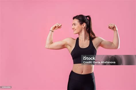 아름 다운 의 절반 길이 초상화 펌핑 여자 에 검은 꽉 끼는 상단과 레깅스 미소와 보여주는 그녀의 큰 그녀의 팔에 근육을 펌핑 포토 스튜디오에서 분홍색 배경에 고립 가냘픈에