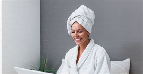 호텔 방의 침대에 수건을 두른 젊은 아름다운 여자 흰색 테리 목욕 가운을 입고 노트북 컴퓨터에서 이메일을 확인하고 얼굴에 약간의 미소를 지었다 사진 Unsplash의