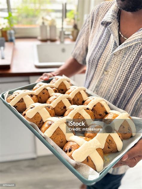 기름칠이 되지 않는 양피지가 늘어선 베이킹 트레이와 부활절 핫 크로스 롤빵이 줄지어 있는 알아볼 수 없는 남자의 클로즈업 이미지