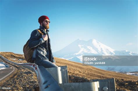 길가 범프에 앉아서 눈 덮인 산의 배경에 대해 석양 배낭 선글라스에 수염된 관광 Hipster 남자 가까운에 대한 스톡 사진 및 기타 이미지 Istock