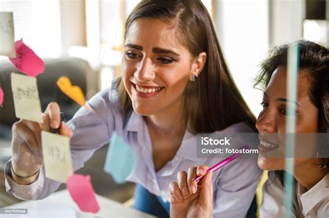 두 명의 창의적인 사업가가 유리 벽에 스티커 메모를 하고 아이디어를 브레인스토밍하고 있다 25 29세에 대한 스톡 사진 및 기타 이미지 25 29세 2명 개념