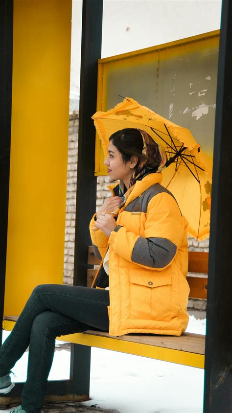 노란 코트와 파란 데님 청바지를 입은 여자가 노란 콘크리트 벤치에 앉아 있다 사진 Unsplash의 무료 의류 이미지