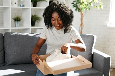 젊은 아프리카 여자는 온라인 구매와 함께 소포 골판지 상자의 포장을 풀기 집에서 소파에 앉아 20 24세에 대한 스톡 사진 및