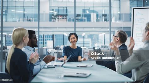 현대 사무실 회의실 아름다운 아시아 전무 이사가 컨퍼런스 테이블의 머리에 앉아 비즈니스 인물 관리자 및 투자자 그룹과 대화를 나누고 있습니다 사람들은 박수를 보냅니다