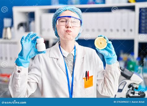 Beautiful Woman Working At Scientist Laboratory Holding Pills And Lemon Puffing Cheeks With