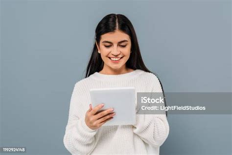 회색에 고립 된 디지털 태블릿을 사용하여 흰색 스웨터에 미소 예쁜 갈색 머리 소녀 갈색 머리에 대한 스톡 사진 및 기타 이미지 갈색 머리 디지털 태블릿 사용하기 무선