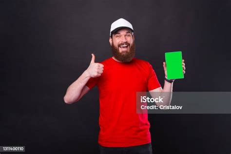 턱수염을 가진 젊은 남자가 엄지 손가락으로 제스처와 태블릿에 녹색 화면을 보여주는 빨간 티셔츠를 입고 놀랐습니다 T 셔츠에 대한 스톡 사진 및 기타 이미지 Istock