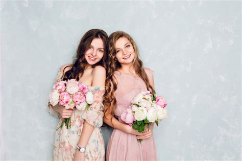 Dos Hermosas Chicas Se Paran En Un Estudio Y Sostienen Ramos De Flores Foto Gratis