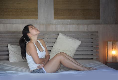 젊은 아름 답 고 예쁜 아시아 중국 여자 아픈 느낌과 복 부와 복 부 경련 및 월 경 생리통 여성 건강 개념에 그녀의 배를 잡고 고통 몸이 침대에 누워 갈색 머리에 대한