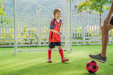 빨간 축구 유니폼을 입은 귀여운 소년과 그의 트레이너 또는 아버지가 야외에서 축구 축구를 하고 있다 아이들이나 아빠와 함께 스포츠를 하는 활동적인 아이 여름에 즐거운 미소를