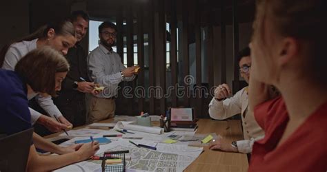 Multicultural Business Team Collaborates On A Project Using Sticky Notes And Blueprints Stock