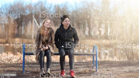 한 쌍의 젊은이들이 공원에서 만났습니다 연인은 도시의 가을 공원에서 벤치에 앉아있다 공원 벤치에 앉아 있는 아시아 소년과 백인 소녀 가을에 대한 스톡 사진 및 기타 이미지