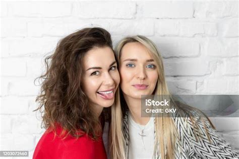 두 젊은 성인 백인 여자 친구 재미와 실내 흰색 벽돌 벽에 대 한 함께 시간을 보내고 즐길 수 있습니다 집에서 소셜 네트워크에 대한 사진을 만드는 속임수와 바보 친구의 쌍