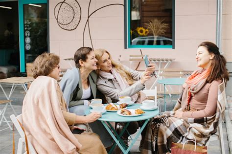 카페 테라스에서 테이블에 커피를 마시고 셀카 사진을 찍는 동안 스마트 폰 카메라에 미소 짓는 세 명의 백인 예쁜 선배 여성 친구 노인은 전화에 포즈 연금 수령자들은 쉬고