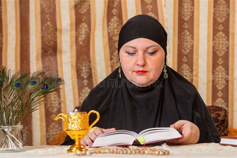 A Muslim Woman In A Black Hijab Sits At A Table With Incense And Gives