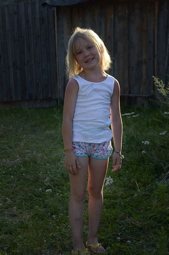 Portrait Of Little Blonde Girl Posing In Farm Yard Summer Village