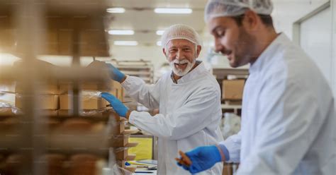 쾌활한 백인 직원들은 흰색 멸균 유니폼을 입고 식품 공장에 서서 상자에 쿠키를 포장합니다 사진 Unsplash의 제조 이미지